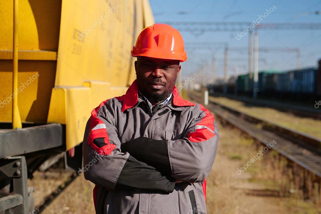 El hombre del ferrocarril con uniforme y sombrero rojo está parado en las vías del ferrocarril ...