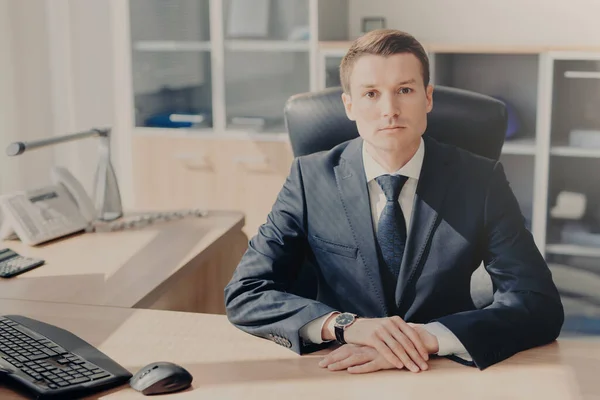 Serious male CEO in formal suit sits at work place in cozy cabinet at ...