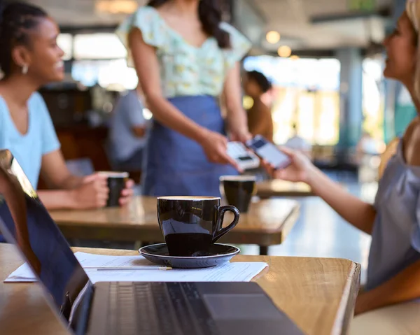 Close Up Of Laptop And Cup In Busy Coffee Shop With Customer Paying ...