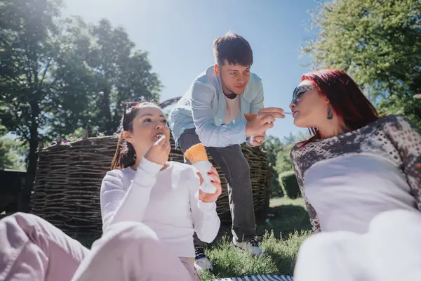 Three friends sharing joy and food on a sunny day outdoors, emphasizing ...