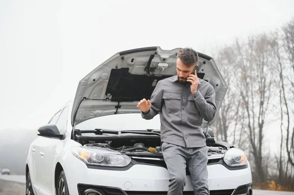 Man use a cellphone call garage in front of the open hood of a broken ...