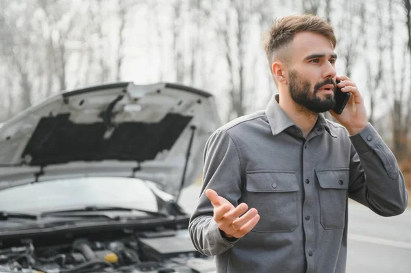 Man use a cellphone call garage in front of the open hood of a broken ...
