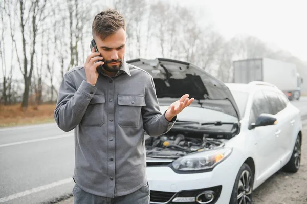 Man use a cellphone call garage in front of the open hood of a broken ...