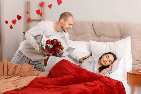 Young Man Greeting His Sleeping Wife With Flowers In Bedroom On Valentines Day Stock Image