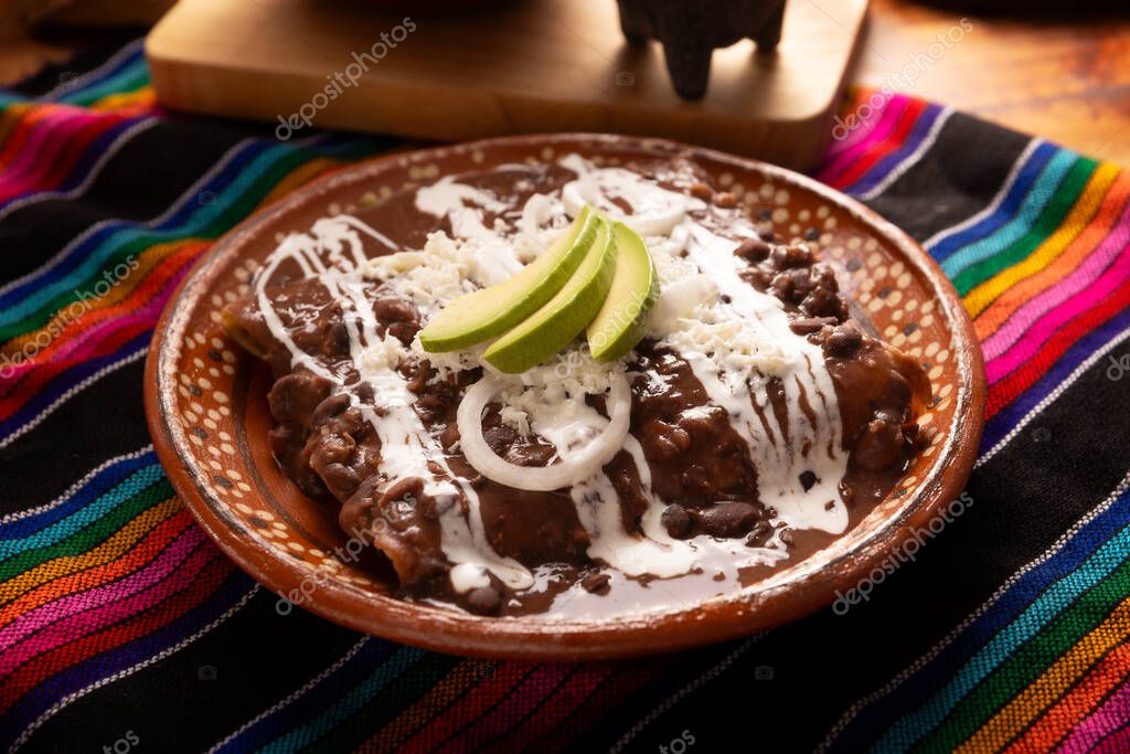 Enfrijoladas. Tortillas de maíz sumergidas en salsa de frijoles, cubiertas de crema y queso, se ...