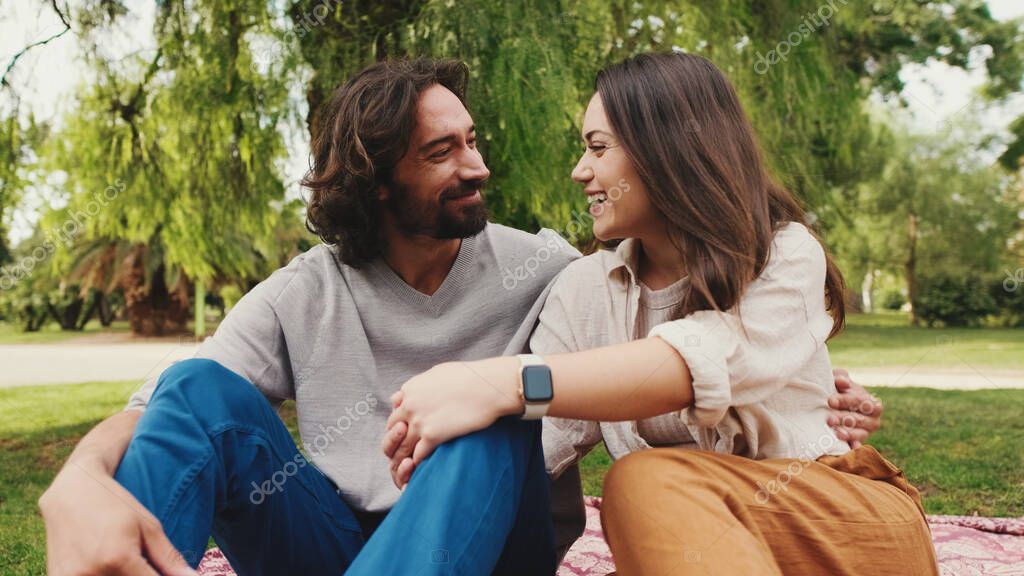 Feliz pareja sonriente hablando mientras está sentada en una manta en ...