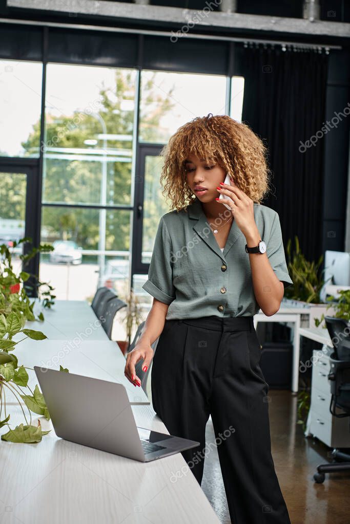 Multi-tasking joven mujer de negocios afroamericana con el ordenador portátil tomando la llamada ...