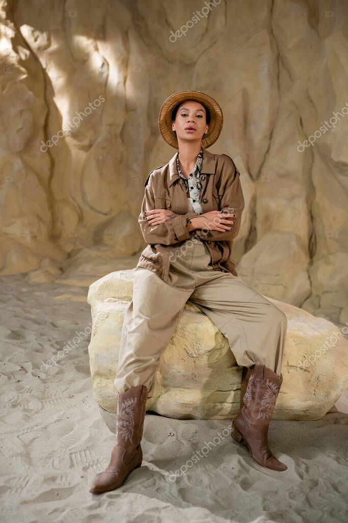 joven arqueólogo en traje de safari sentado en piedra con los brazos ...