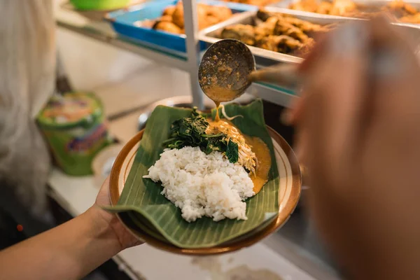 mano verter salsa de maní en el arroz vegetal pecel en un puesto de ...