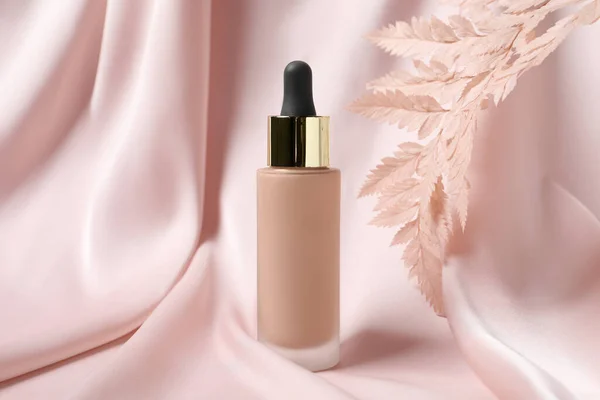 Bottle of skin foundation and decorative plant on pink cloth. Makeup ...