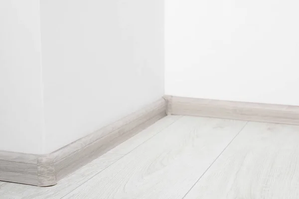 Plinto de madera con conectores en suelo laminado cerca de pared blanca ...