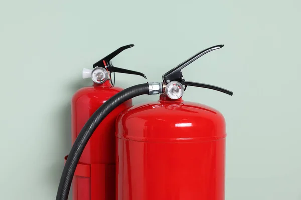 Red fire extinguishers against light green background, closeup - Stock ...