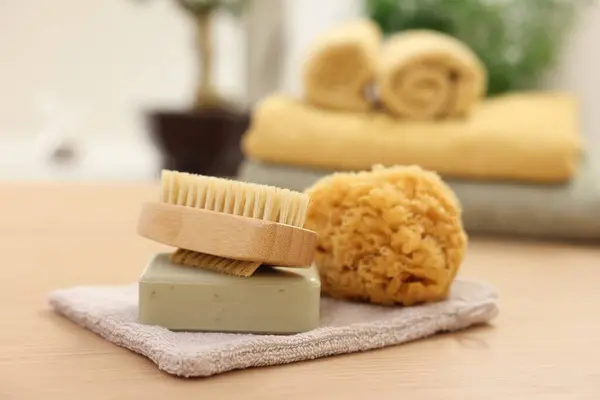 Soap bar, brush and natural sponge on light wooden table, closeup. Spa ...