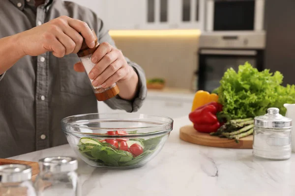 Cooking process. Man adding salt into bowl of salad at white marble ...