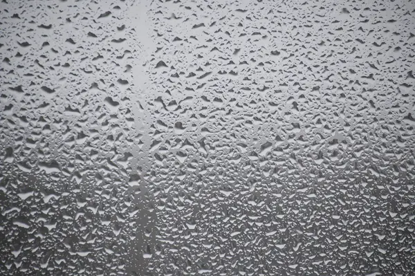 Raindrops on a window, precipitating from a drizzle outside, create a ...