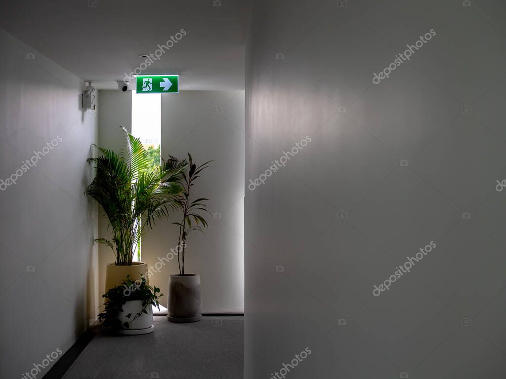 Green fire escape sign hang on the ceiling at the corner of corridor in ...