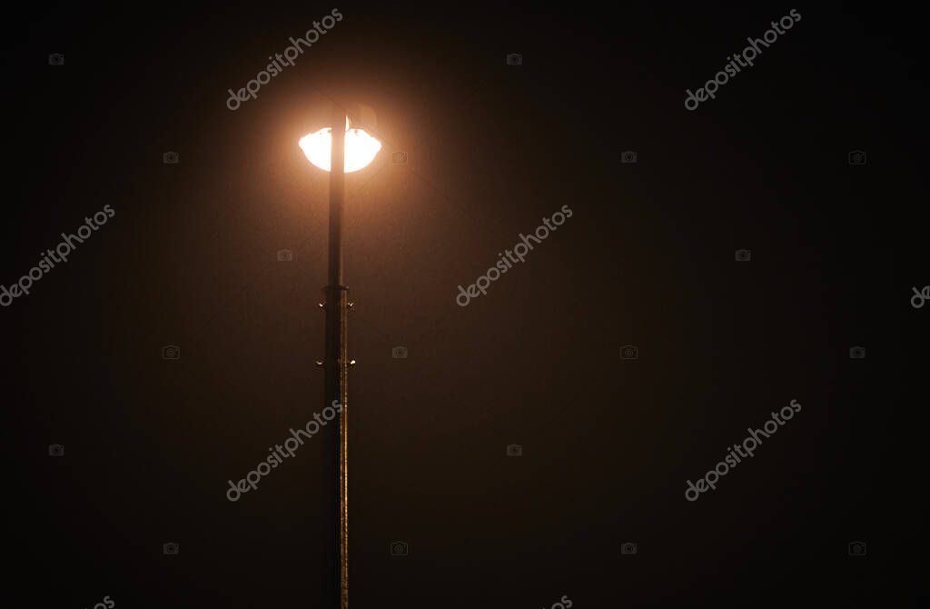 One night lamppost shines with faint mysterious yellow light through ...