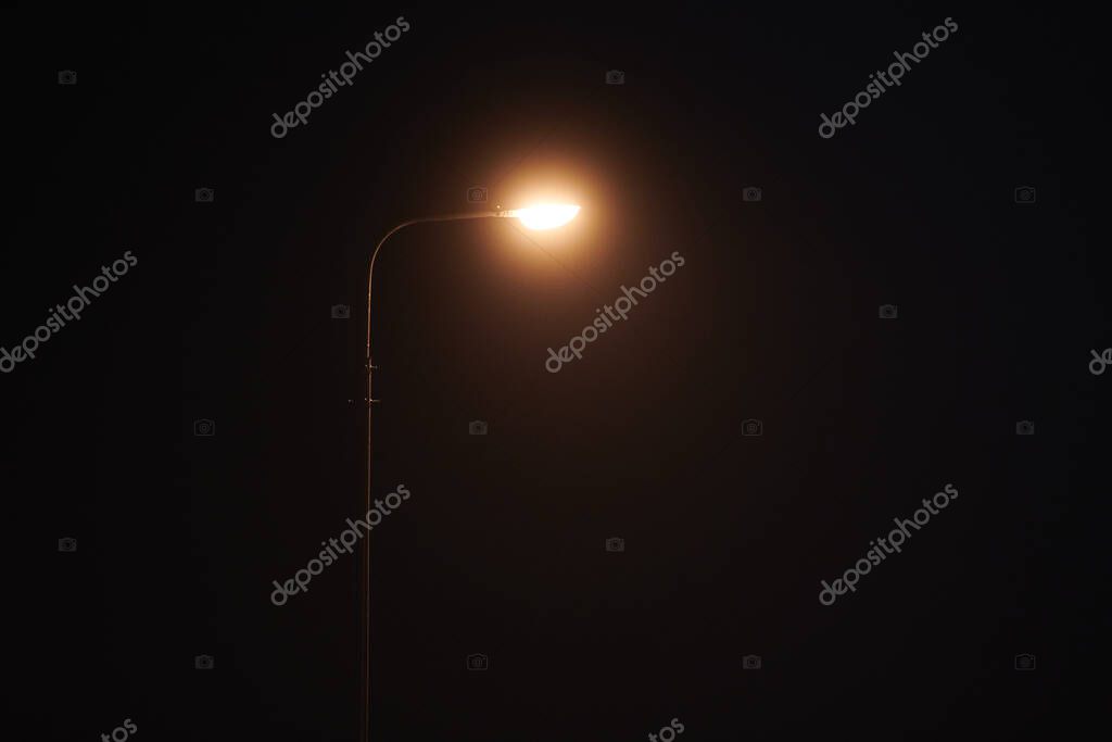 One night lamppost shines with faint mysterious yellow light through ...