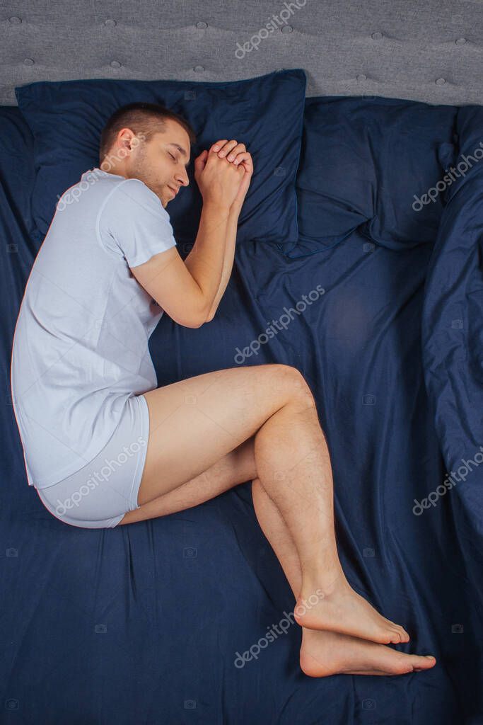 Handsome young man sleeping comfortably on the bed at night in his bedroom wearing pajamas ...