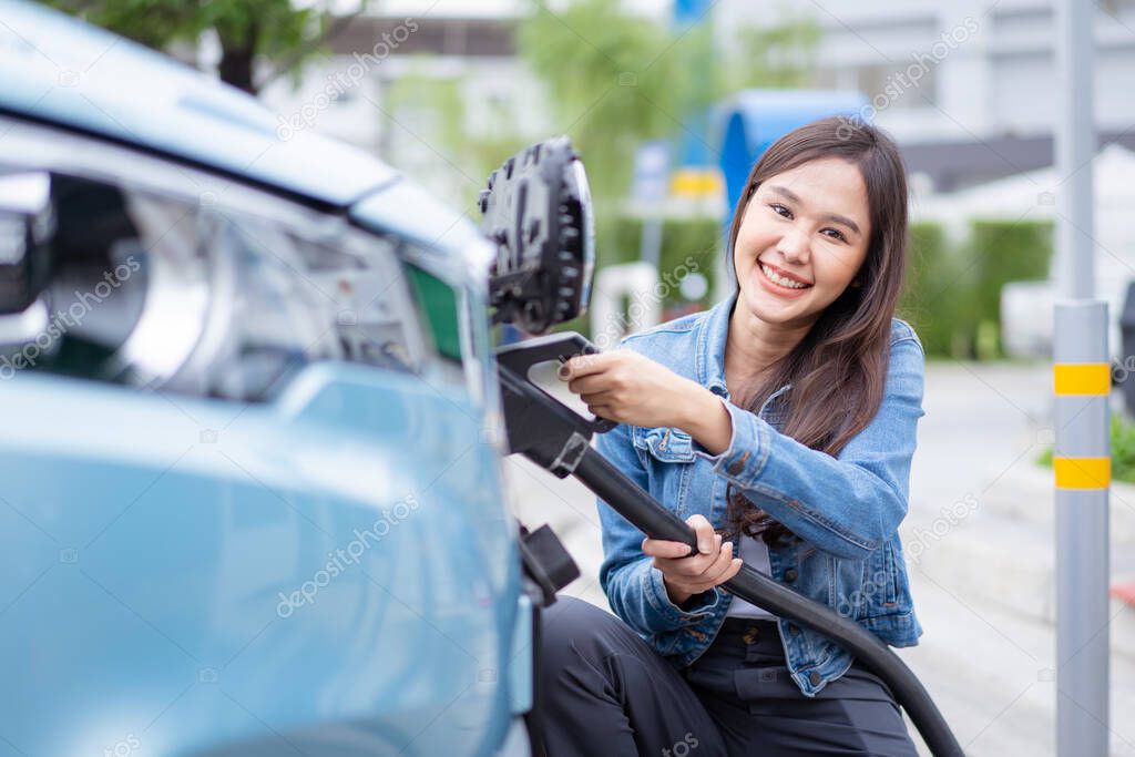 Hermosa mujer asiática que conecta un conector de carga DC CCS2 EV a un vehículo, mujer que ...