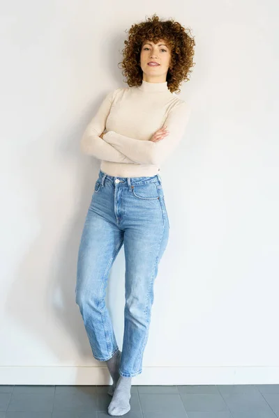 Full body of curly haired female in jeans and beige turtleneck leaning ...