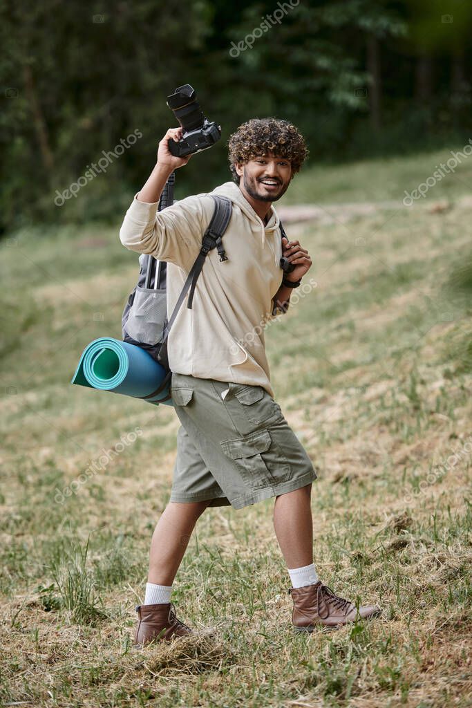 alegre turista indio caminando en el bosque y sosteniendo la cámara ...