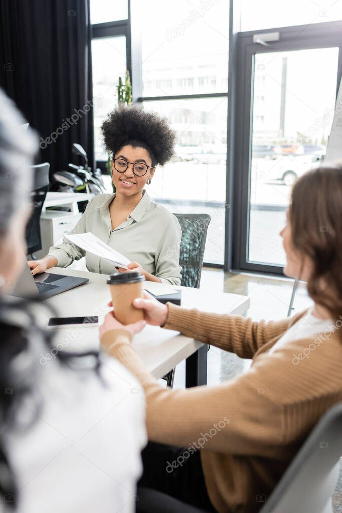 feliz mujer de negocios afroamericana hablando con una colega con café para ir a la oficina ...
