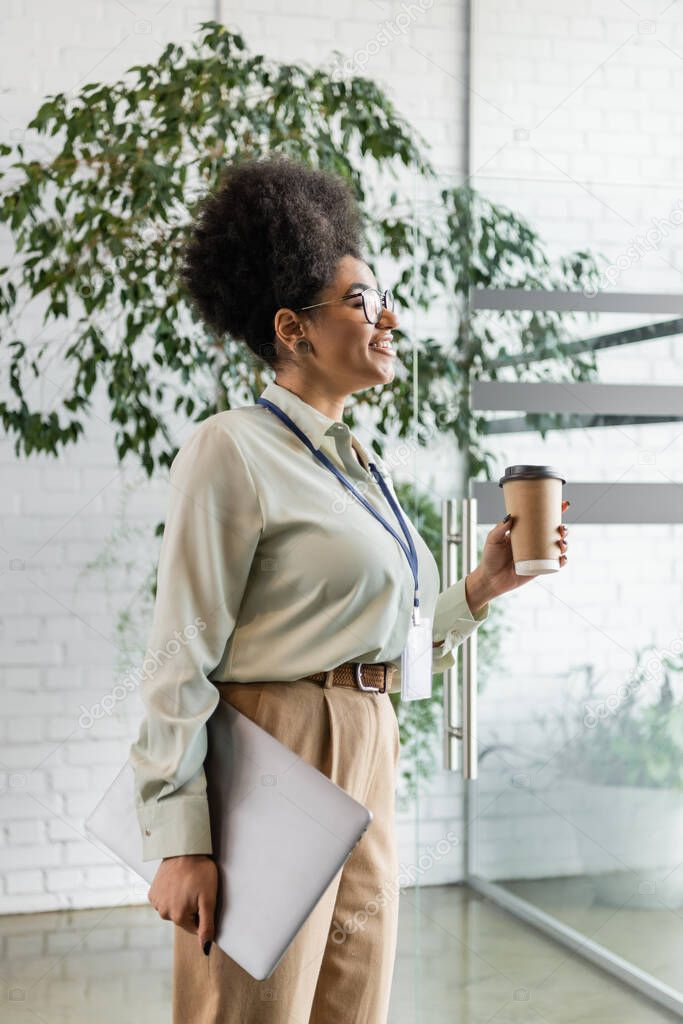 vista lateral de la feliz mujer de negocios afroamericana en gafas con portátil y café para ...