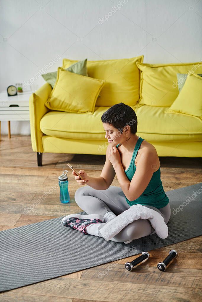 plano vertical de mujer morena bonita sentada en el suelo y mirando el teléfono móvil, fitness 2024