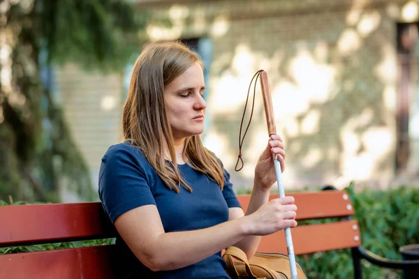 Close-up of a visually impaired woman holding a white cane and sitting ...