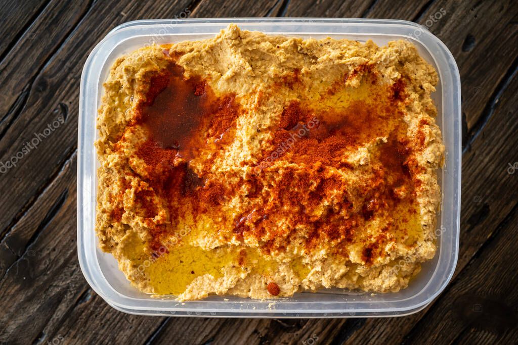 Hummus casero en un recipiente de plástico con pimentón y aceite- 2023