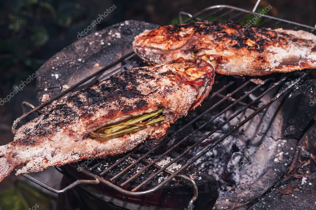 The ruby fish is coated with salt and placed on a charcoal grill in a ...
