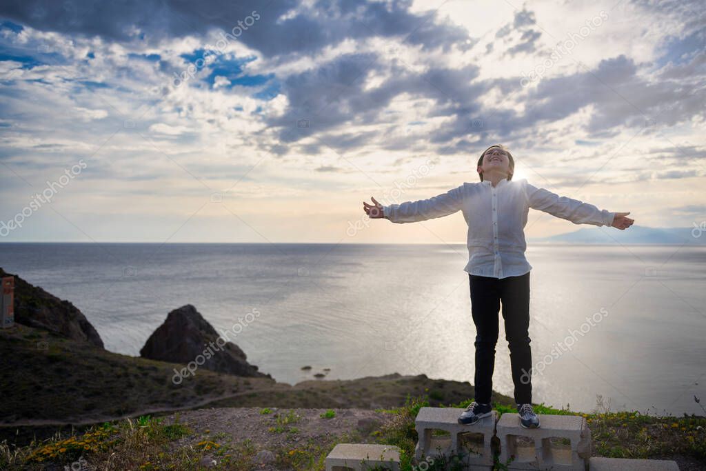 Un niño está parado en un acantilado, con los brazos extendidos hacia ...