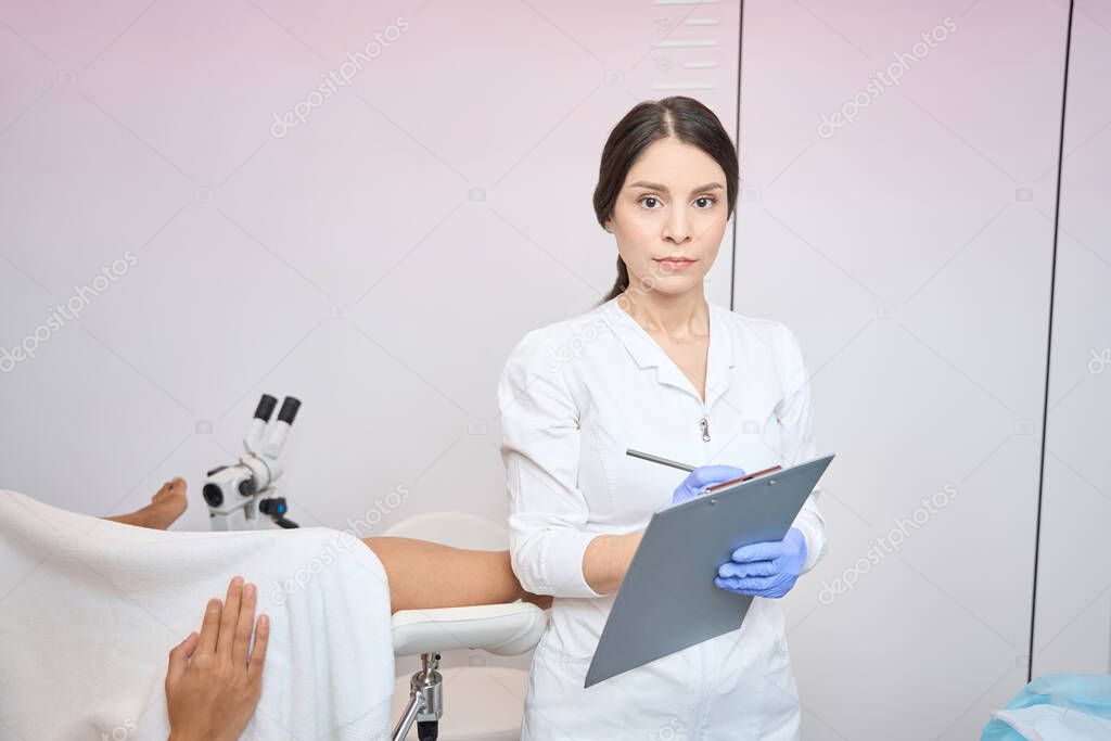 La ginec loga est de pie y anotando las quejas de la paciente en el historial m dico en la cl ...