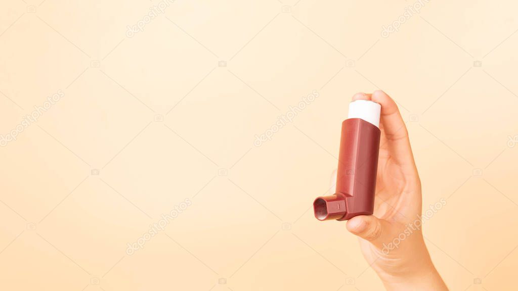 Inhalador de asma marrón de mano sobre fondo naranja. El producto ...