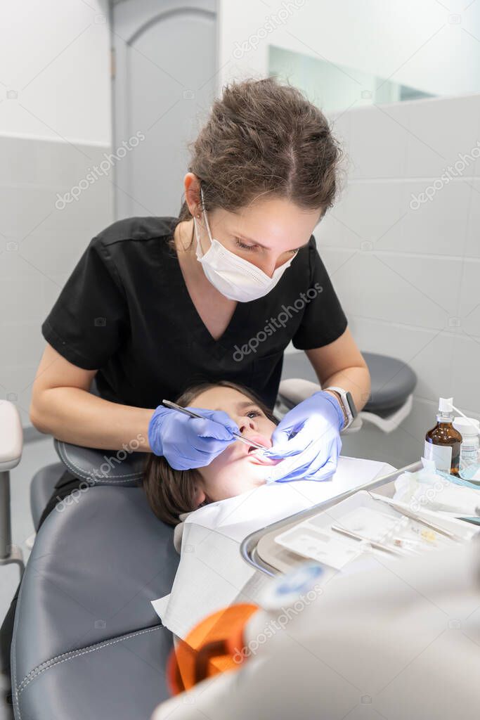 Una dentista pediátrica realiza un examen dental de la cavidad oral de un paciente niño sentado ...