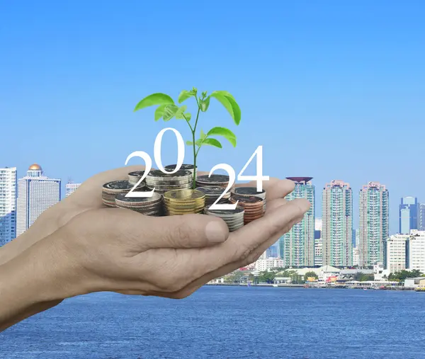 Hands holding growing tree with 2024 white text and coins over city ...