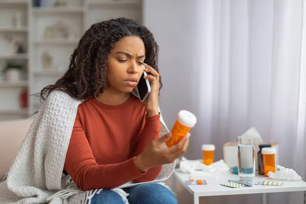 A concerned young black woman holding a prescription bottle and talking ...