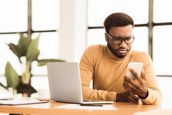 Confused Guy. Black businessman looking at smart phone, surprised by ...