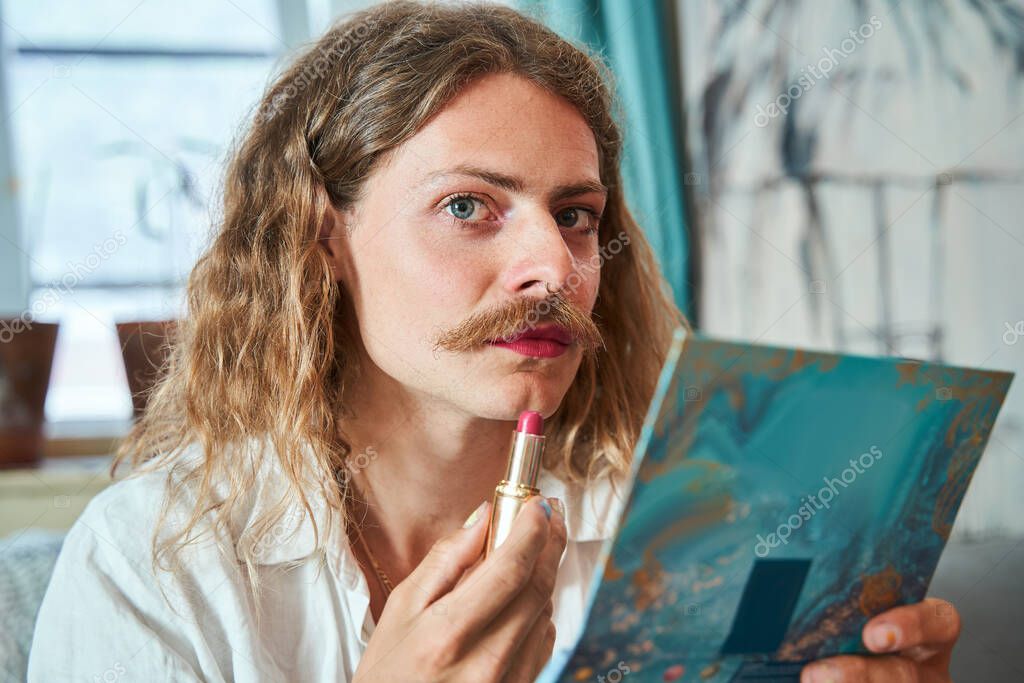 Joven hombre de pelo largo con bigote sosteniendo lápiz labial y ...