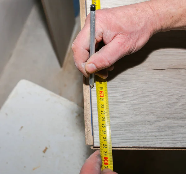 Worker making laminate flooring in apartment. Measure tape and pencil ...