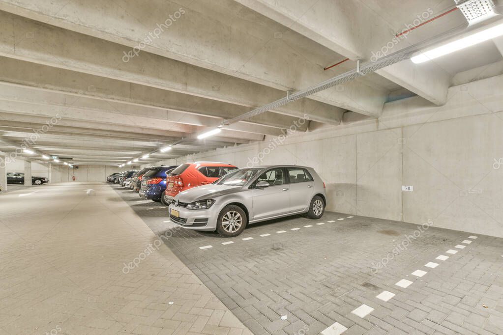una zona de aparcamiento subterráneo con coches aparcados en los garajes y personas caminando en ...