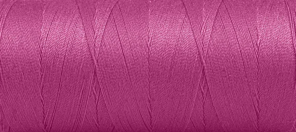 Texture of threads in a spool of pink color on a white background close ...