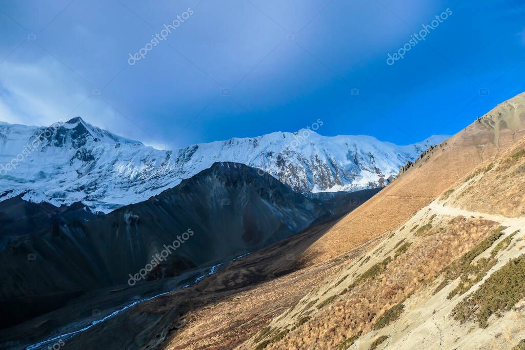 A view on the sunny pathway leading to dark, shadowy mountain peaks ...
