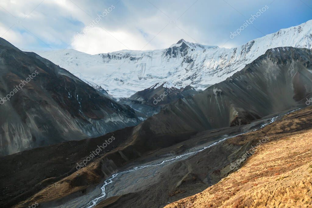 A view on the sunny pathway leading to dark, shadowy mountain peaks ...