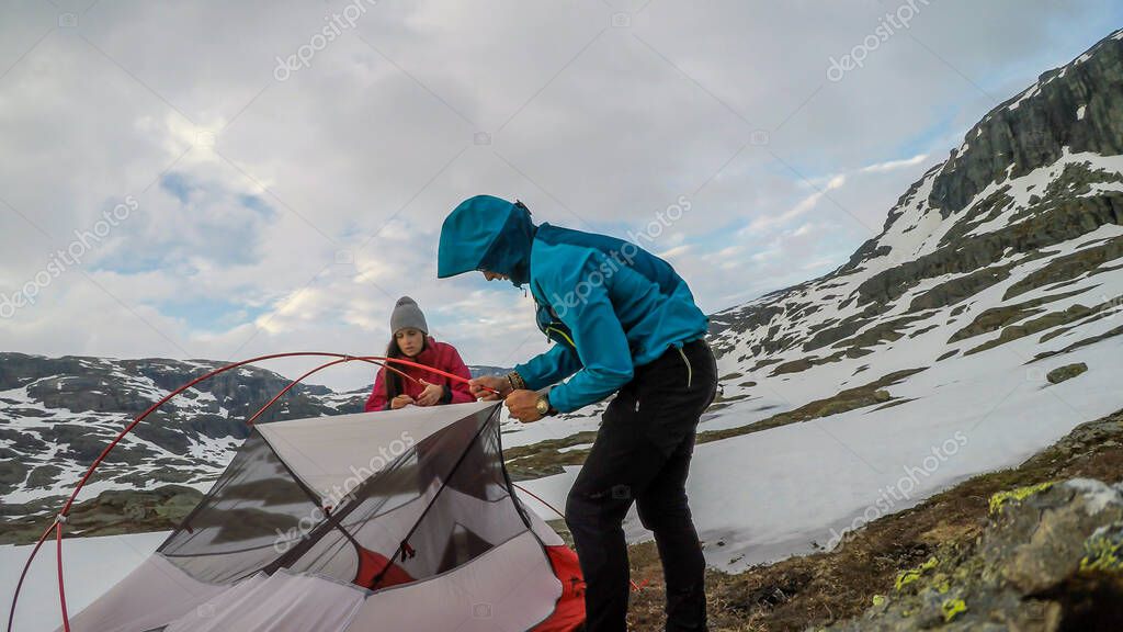 A young couple putting the tent up in the wilderness. The ground is ...