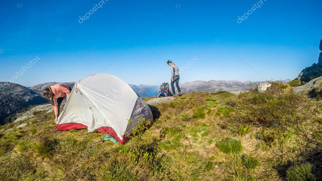 A young couple putting the tent up in the wilderness. The girl ...