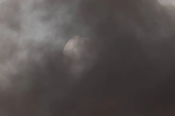Solar eclipse on a cloudy day. Cloudy sky, the sun can be seen from behind a thin layer of ...