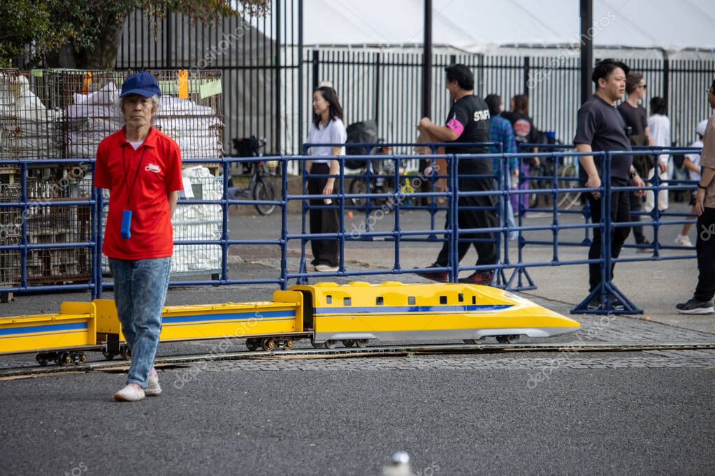 Tokio, Japón, 4 de noviembre de 2023: Trabajador con camisa roja de pie junto al tren modelo ...