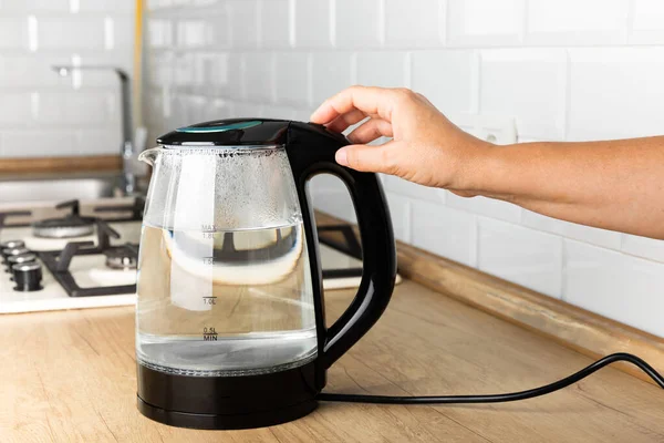 Close-up of a woman pressing the power switch on an electric kettle on ...